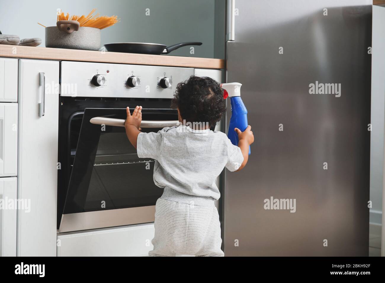 Little African-American baby playing with detergent and oven at home ...