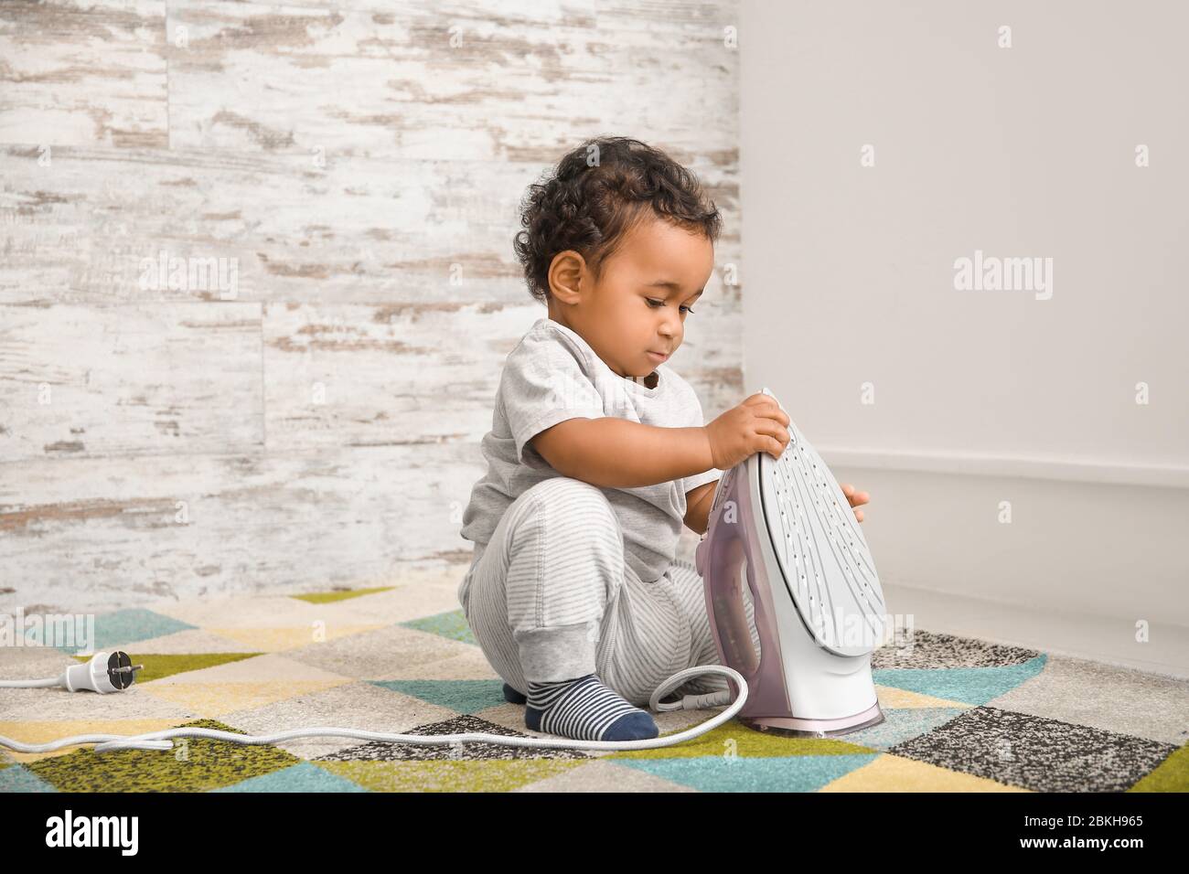 Little African-American baby playing with iron at home. Child in danger ...