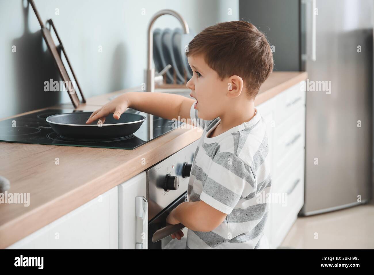 Little boy playing with frying pan on electric stove at home Stock ...