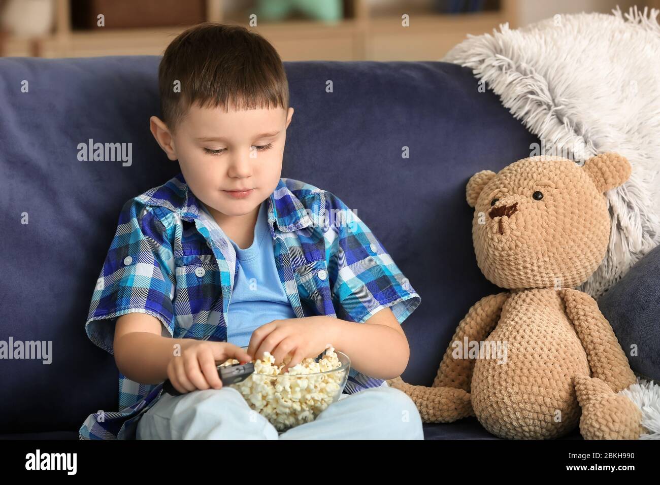 Cute little boy eating popcorn and watching TV at home Stock Photo - Alamy