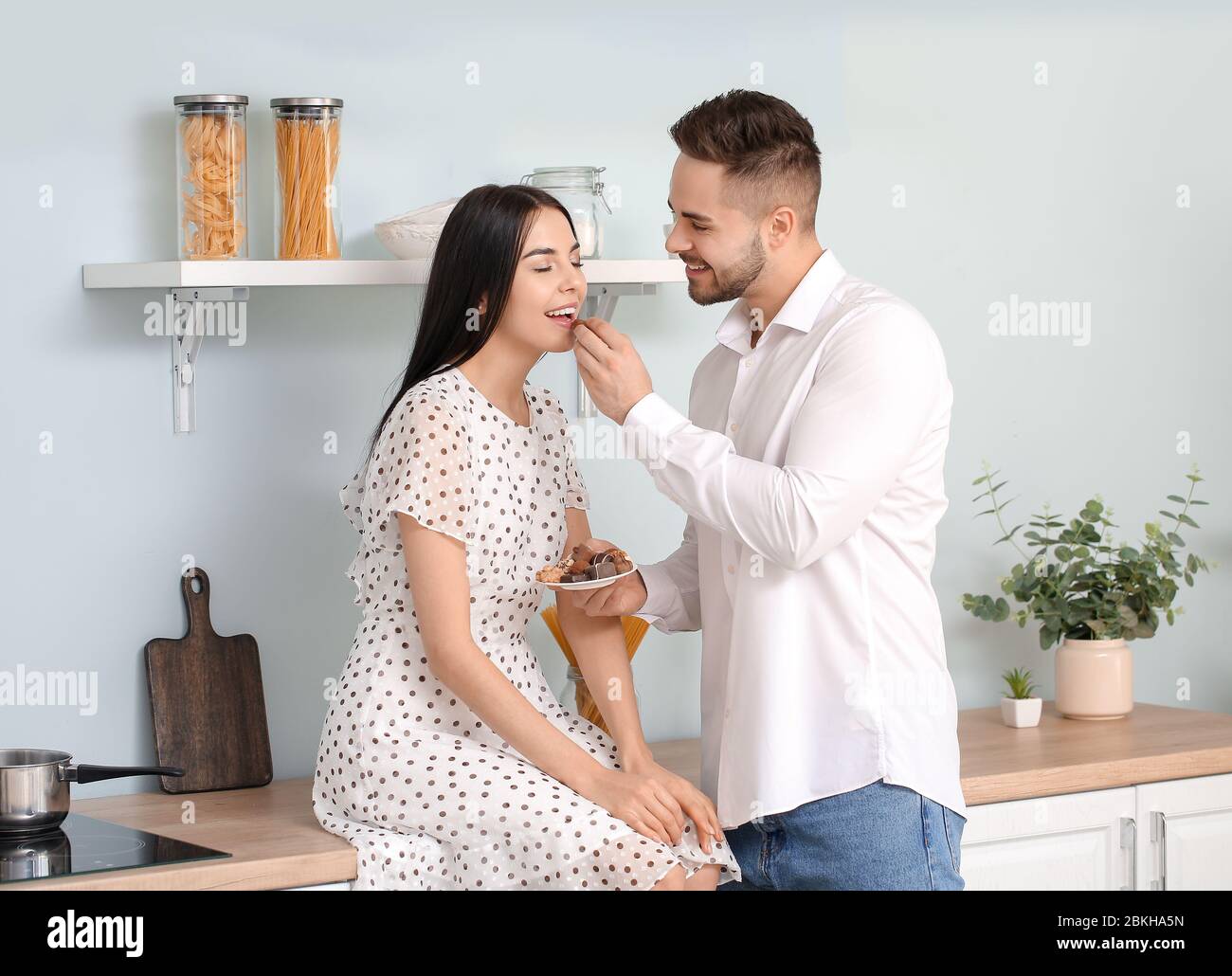 Beautiful young couple eating chocolate in kitchen Stock Photo - Alamy