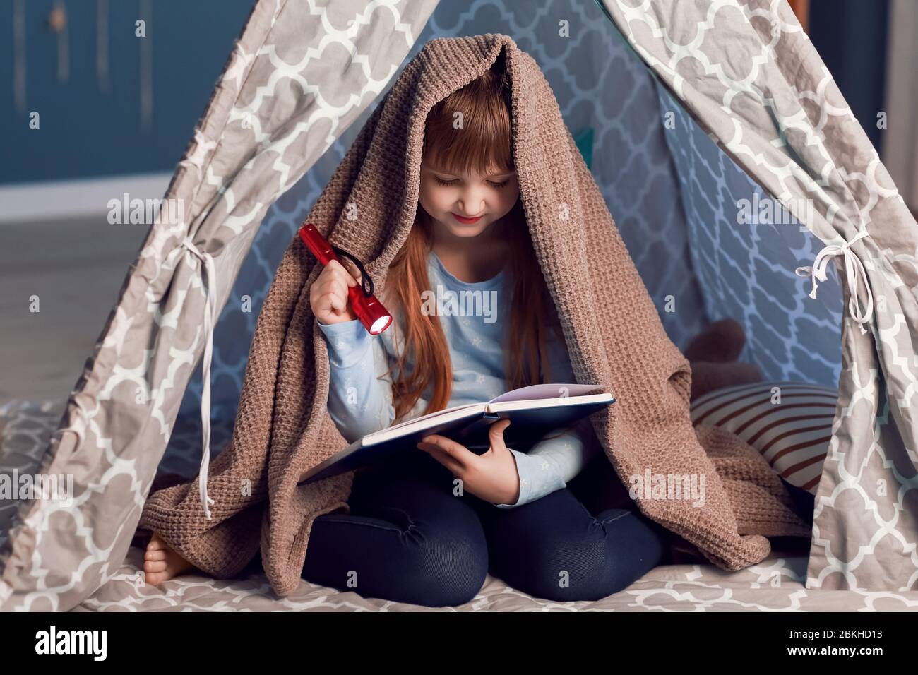 Little girl reading book in play tent at night Stock Photo - Alamy