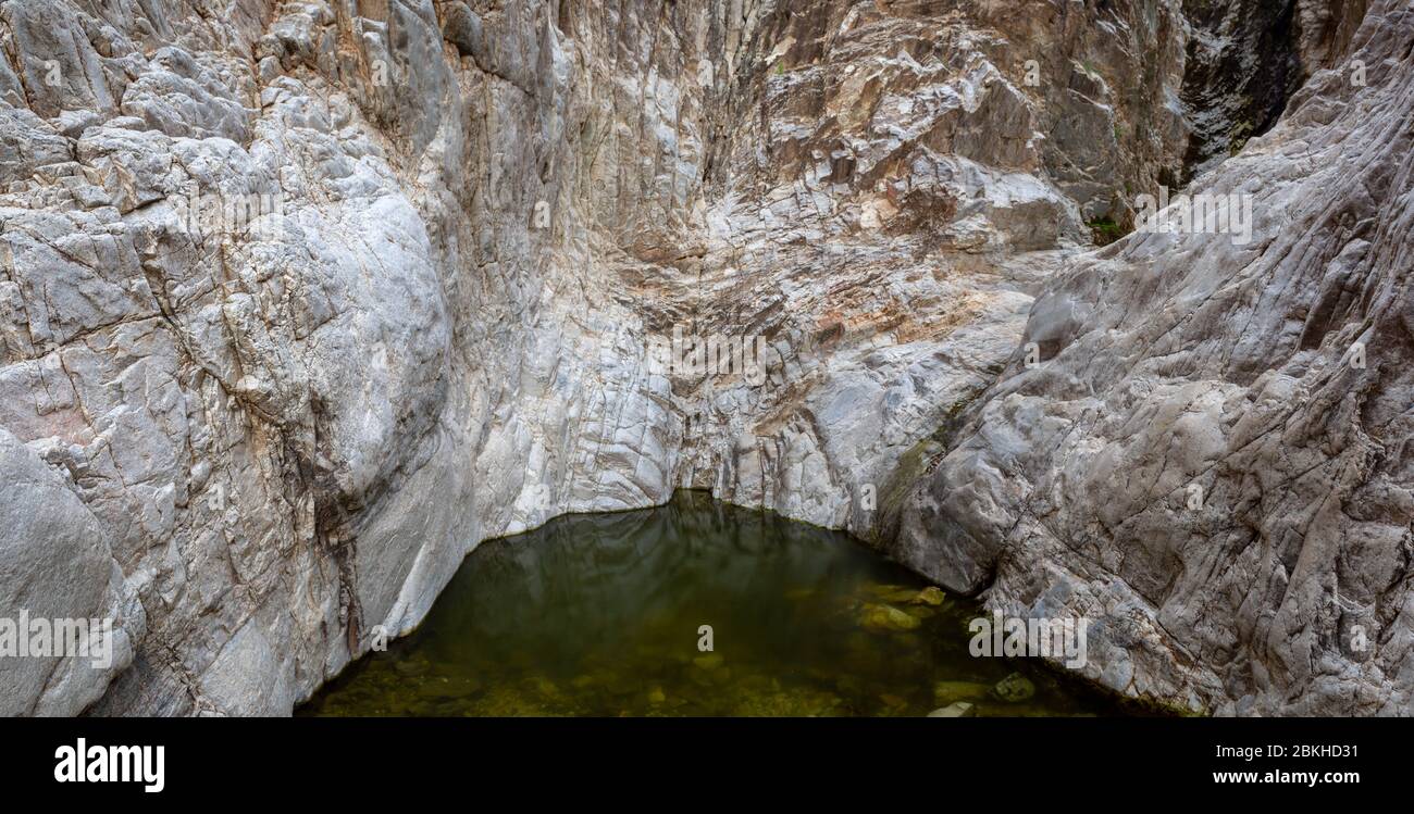 A hidden waterhole with clam water in a canyon with grey rock cliffs ...