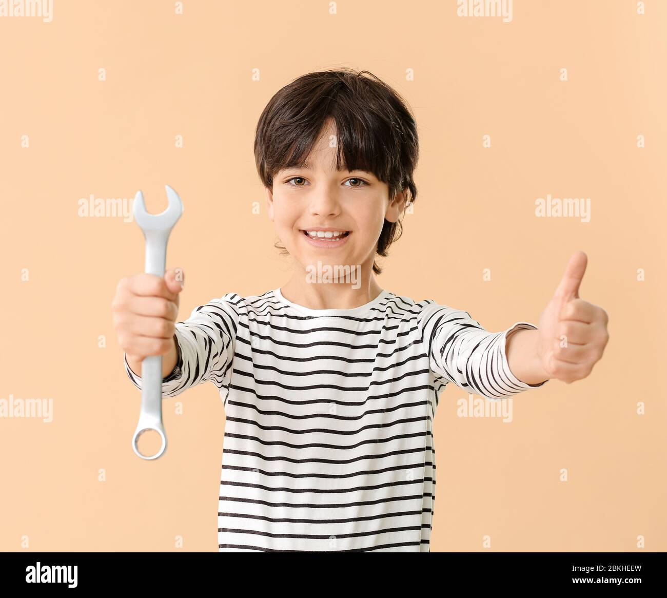 Portrait of little plumber showing thumb-up gesture on color background ...