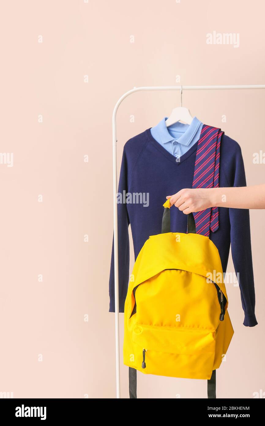 Stylish school uniform hanging on rack and female hand with backpack ...