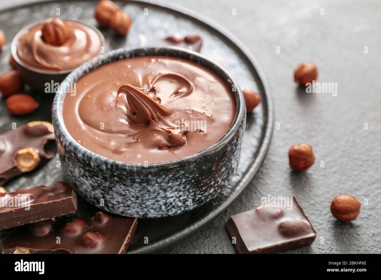 Bowl with tasty chocolate paste and hazelnuts on grey background Stock ...