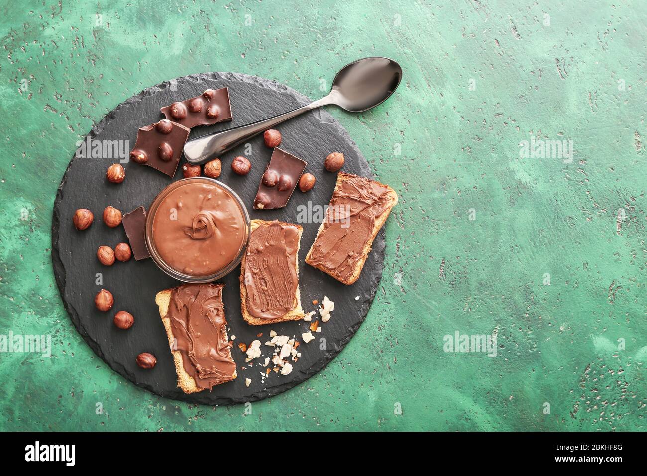 Slate plate with fresh bread and chocolate paste on color background ...
