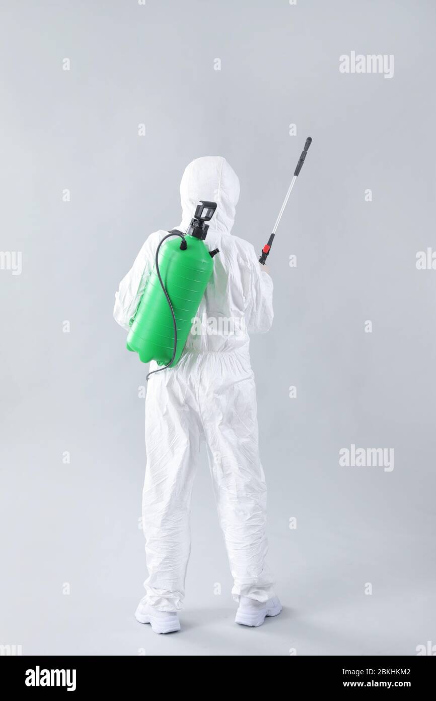 Worker in biohazard suit and with disinfectant on grey background Stock ...