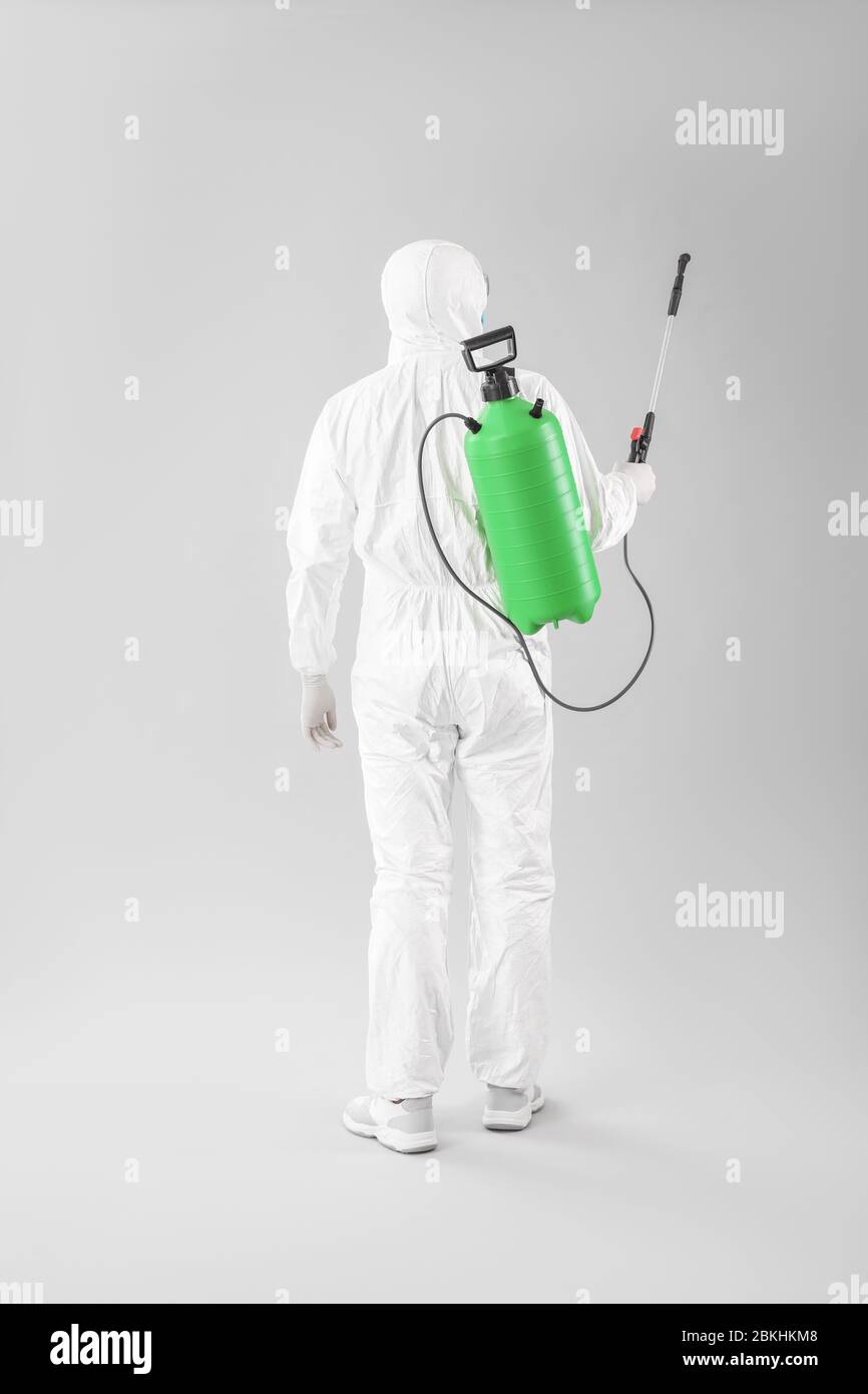 Worker in biohazard suit and with disinfectant on grey background Stock ...