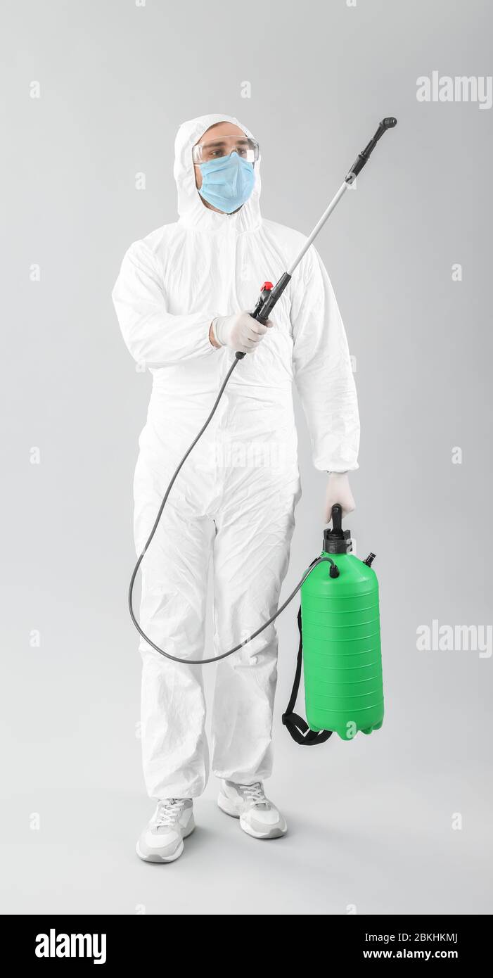 Worker in biohazard suit and with disinfectant on grey background Stock ...