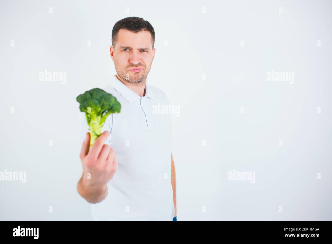 Young man isolated over white background. Guy hold broccoli in hand and ...