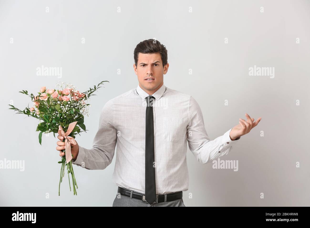 Handsome confused man with bouquet of flowers on light background Stock ...