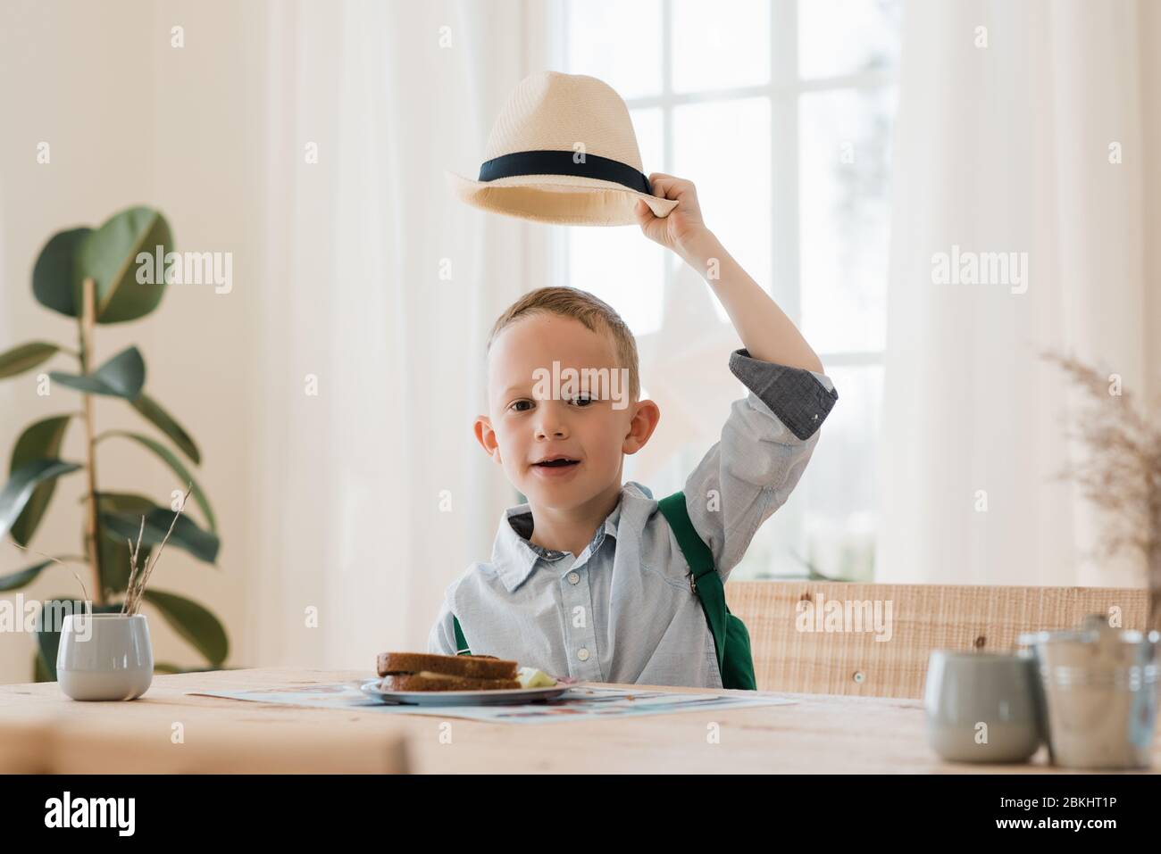 boy holding his hat up whilst eating his lunch at home smiling Stock ...