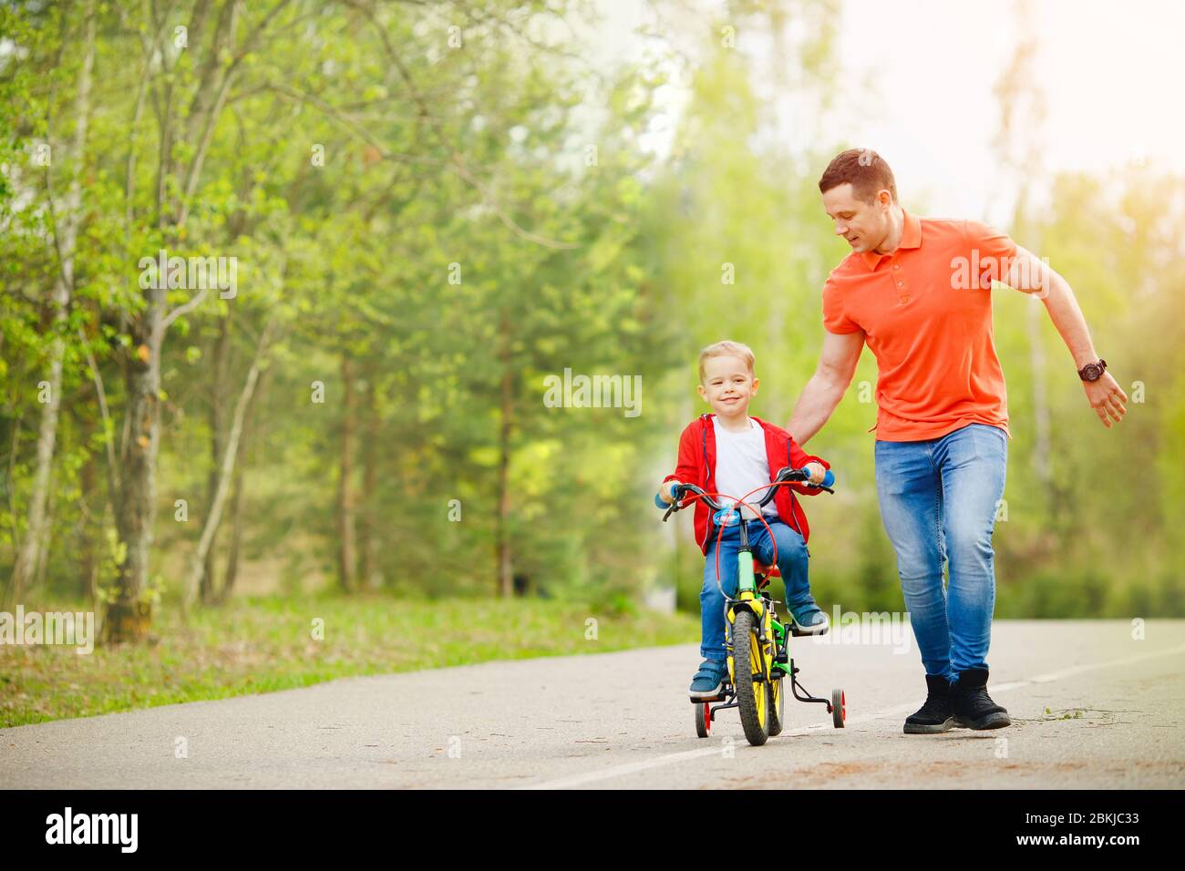 Happy father teaching his little son to ride bicycle. Child learning ...