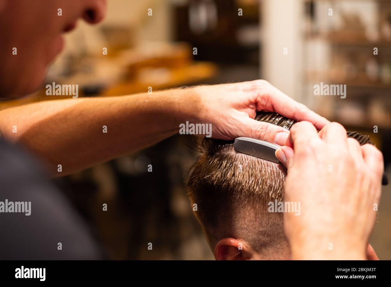 Barber shaves the parting of a young man's hair with a razor blade in ...