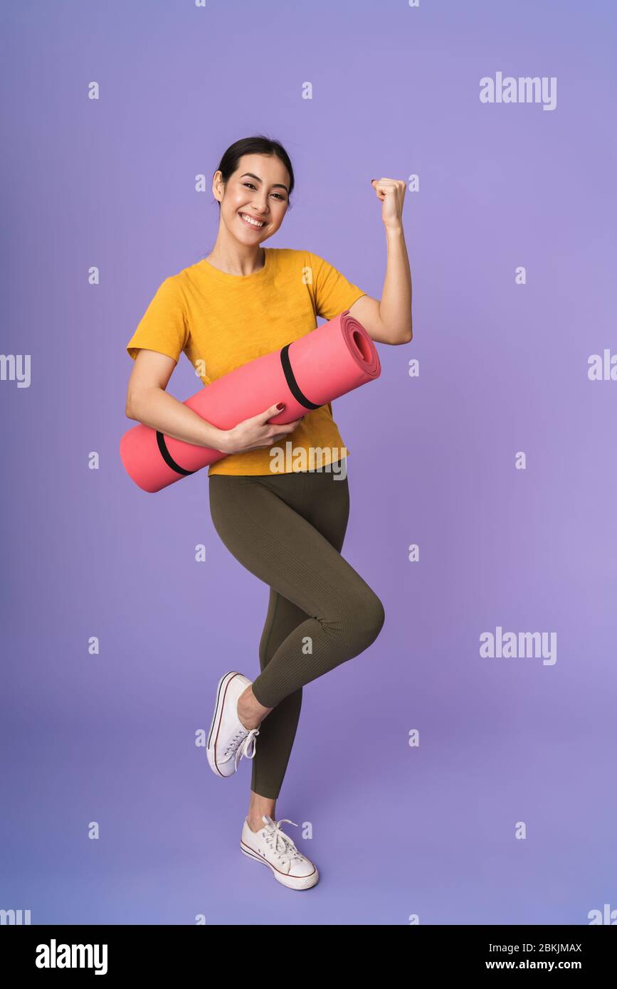 Full length of a cheerful young pretty sportswoman standing isolated over violet background ...