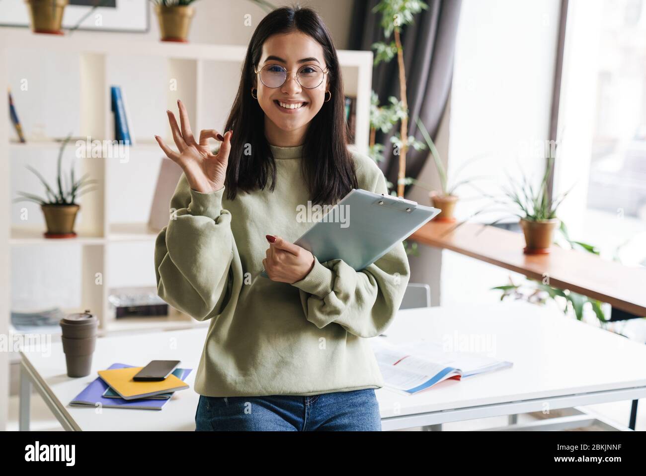Image of a pretty positive happy cheery young girl student indoors ...