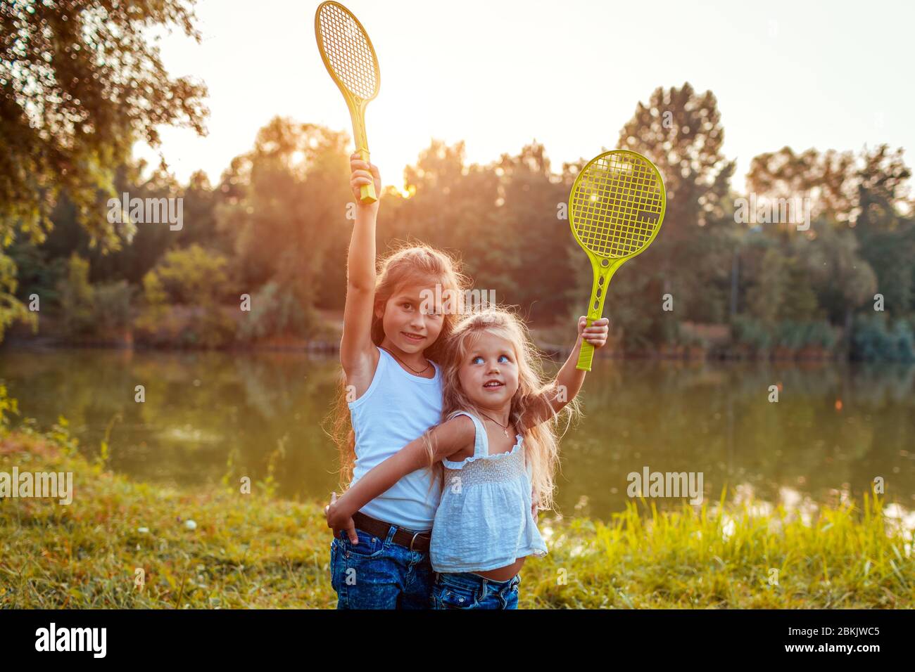 Little girls having fun outdoors after playing badminton. Sisters raise ...