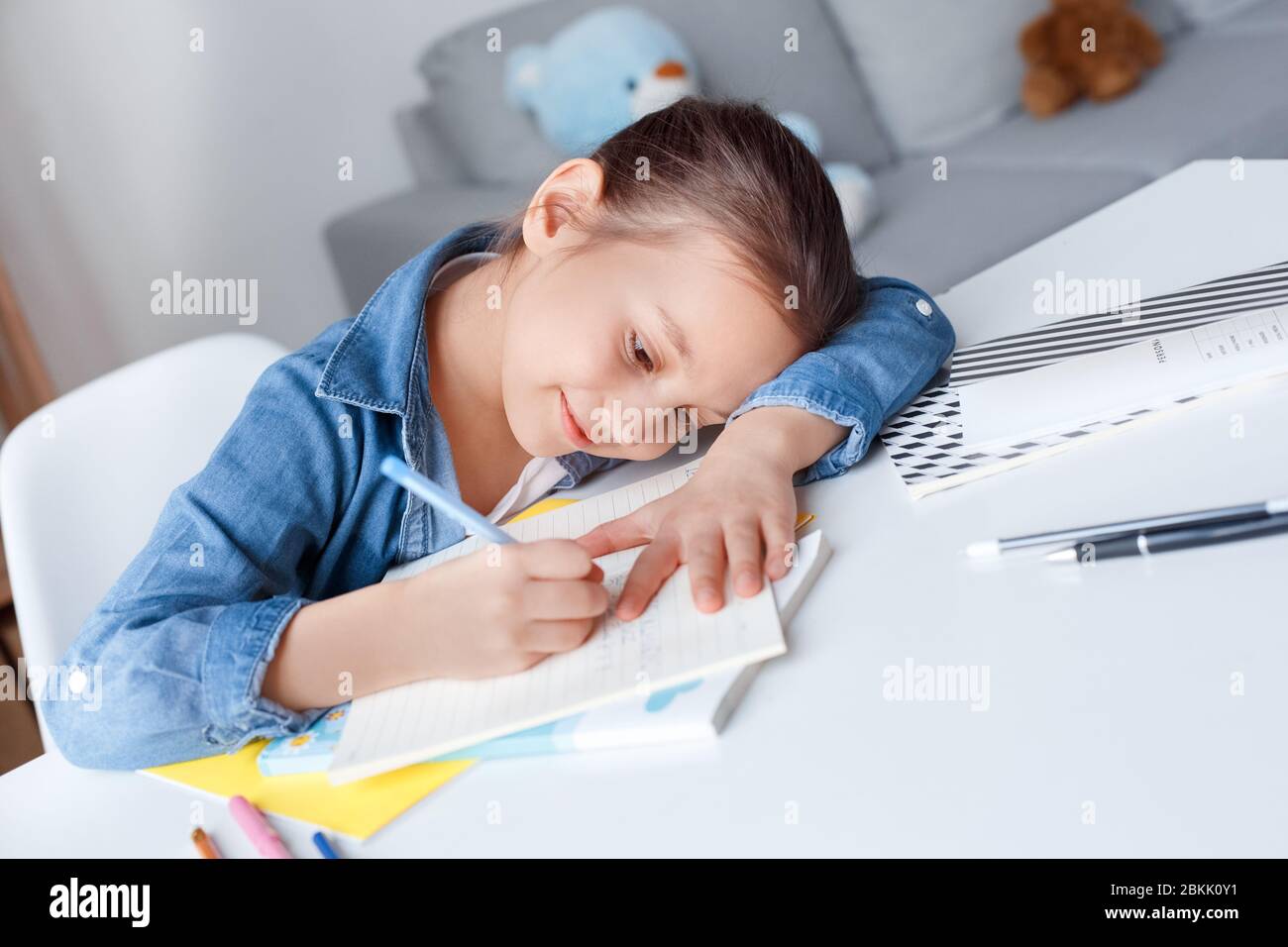 Smiling and preteen girl making homework lessons, sitting behind table ...