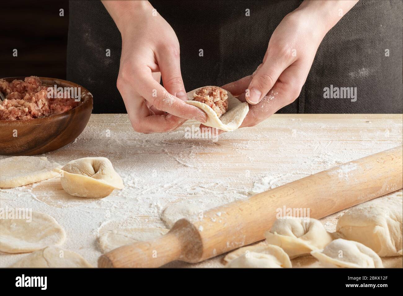Front view of woman's hands making meat dumpling with wooden rolling ...