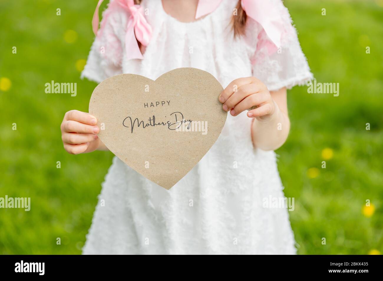 Happy Mother's Day written on a heart-shaped card held by a girl on ...