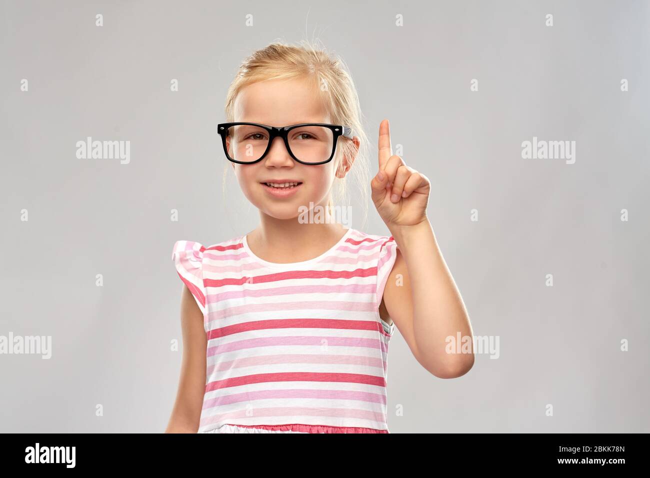 smiling little girl in glasses pointing finger up Stock Photo - Alamy