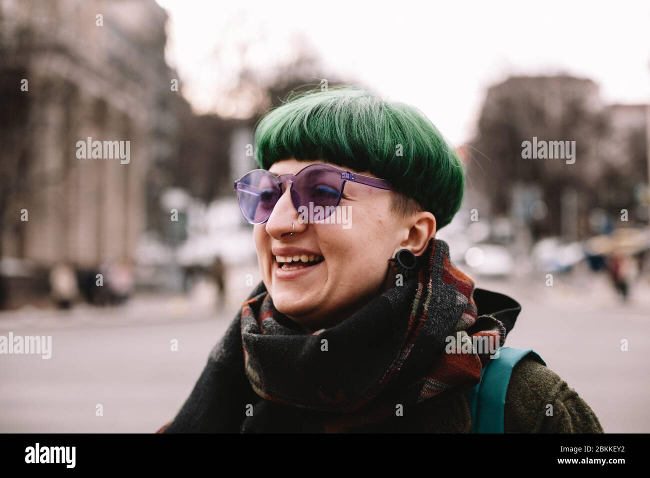 Portrait of happy punk woman in purple sunglasses standing in city ...