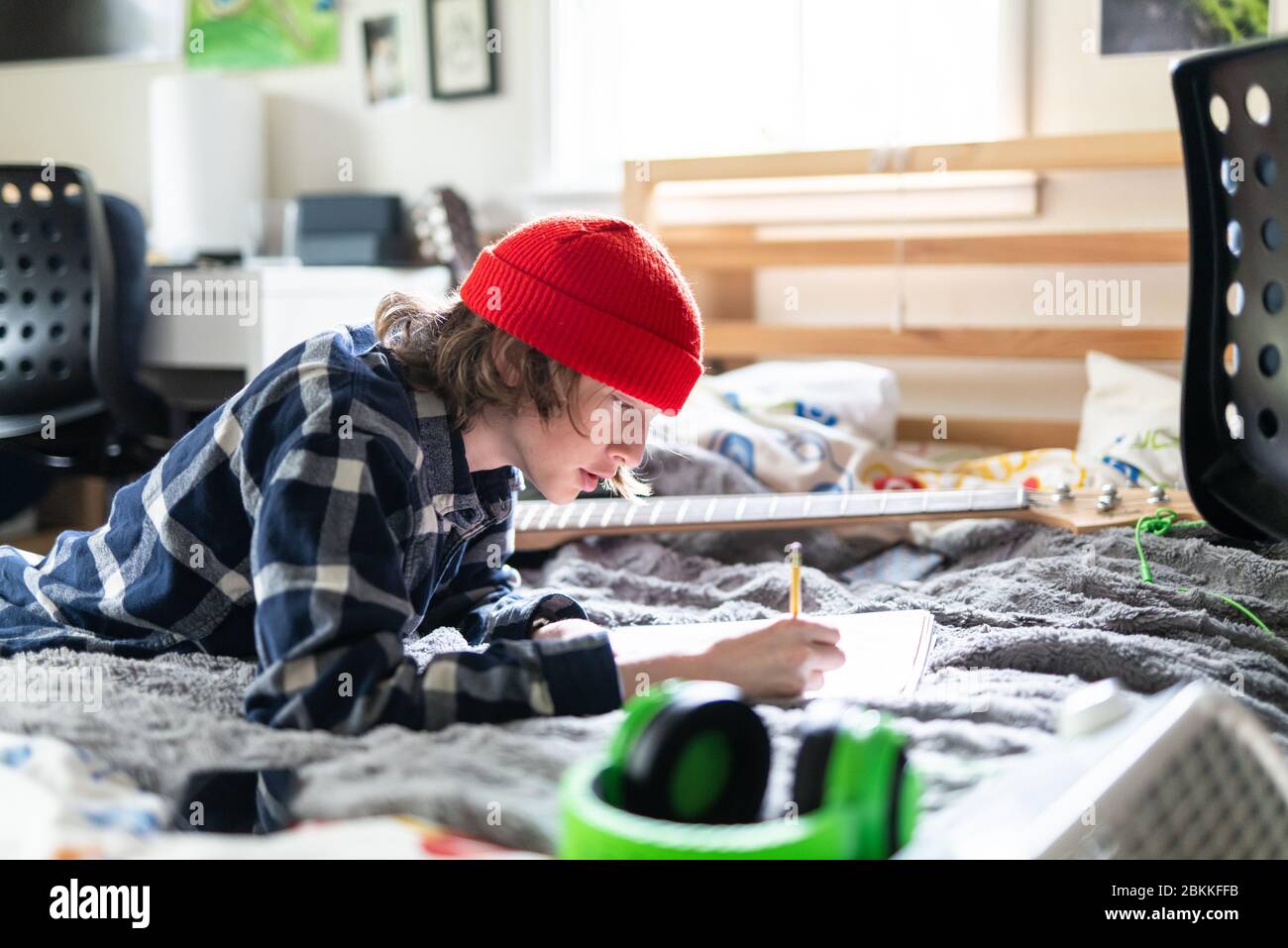 Teenage boy working on homework in bedroom surrounded by belongings ...