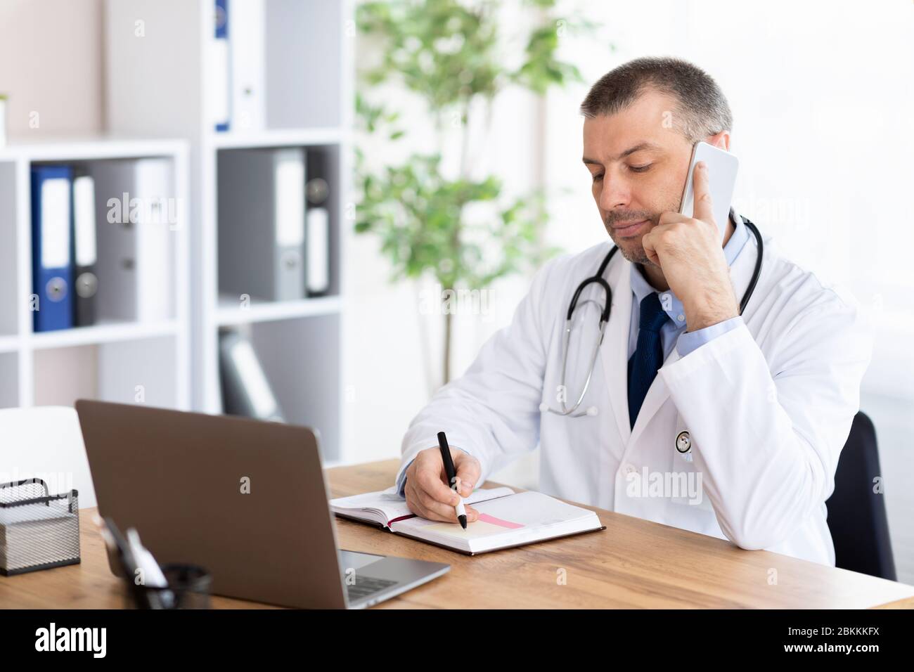 Doctor talking on phone with his patients and writing notes Stock Photo ...