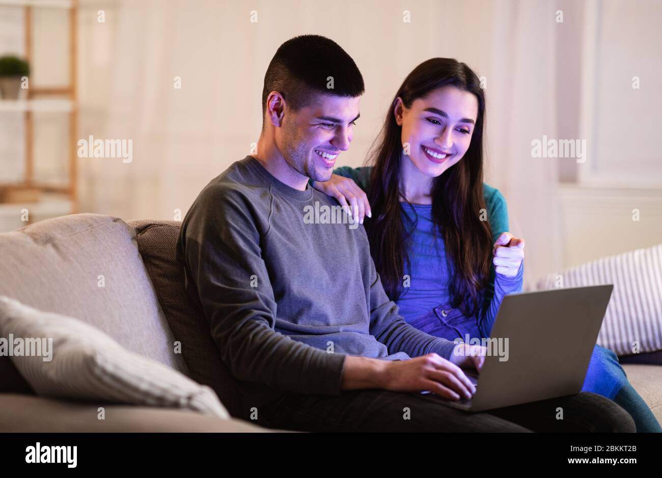 Happy couple using pc sitting on the couch Stock Photo - Alamy