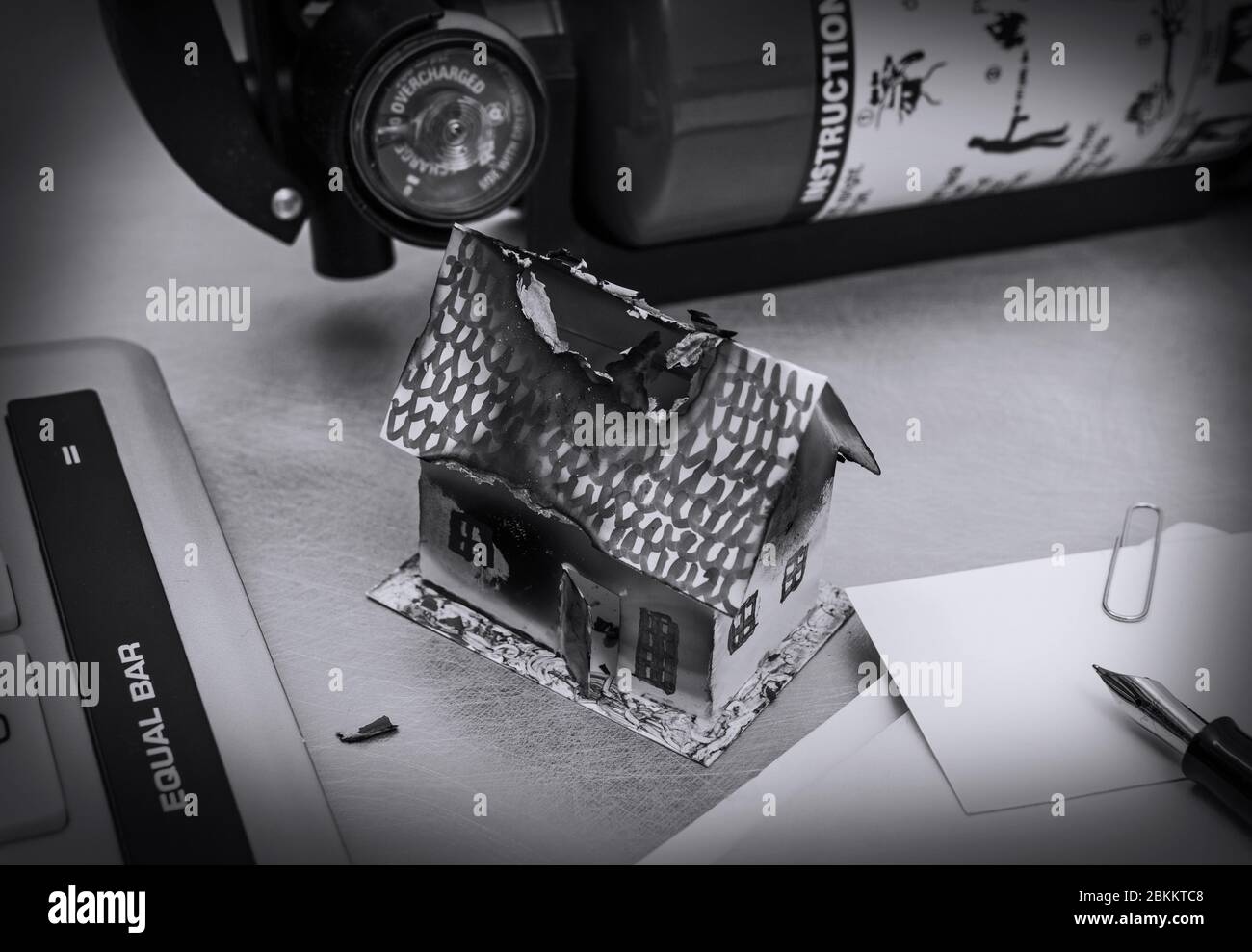 A tiny paper house partially burned, surrounded by a fire extinguisher ...