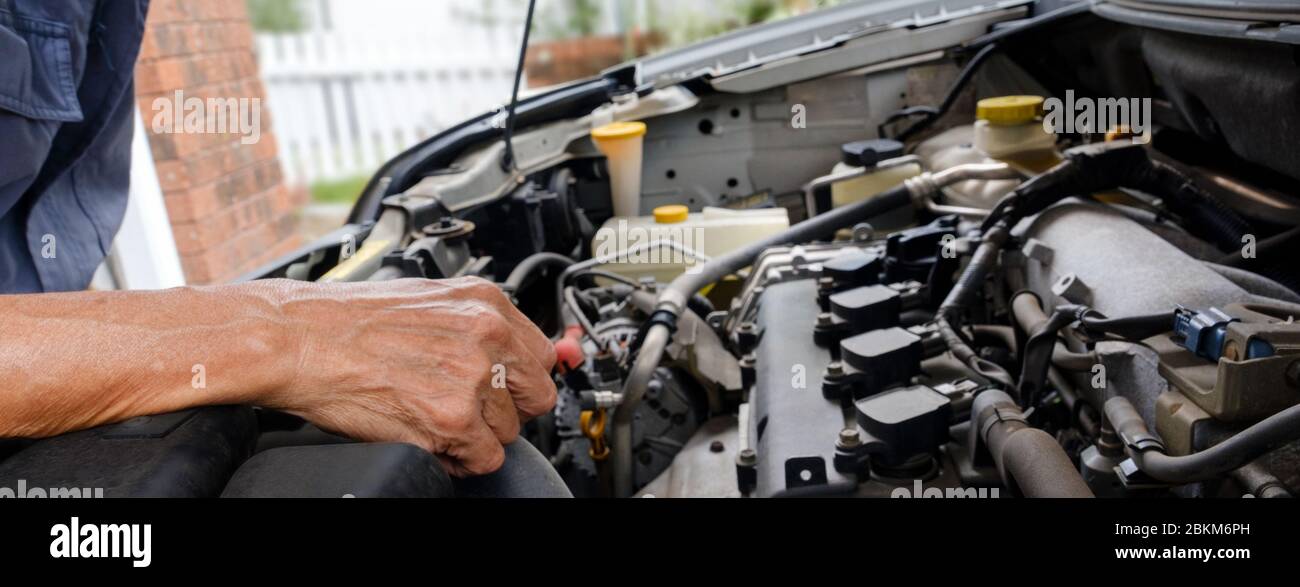Mechanic leans in under the bonnet of a car during a service to look ...