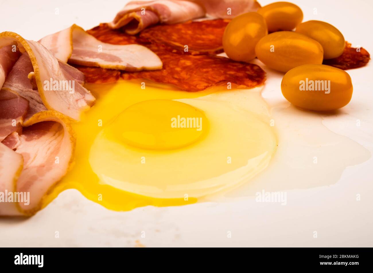 A broken chicken egg without a shell, slices of sausage and bacon and ...