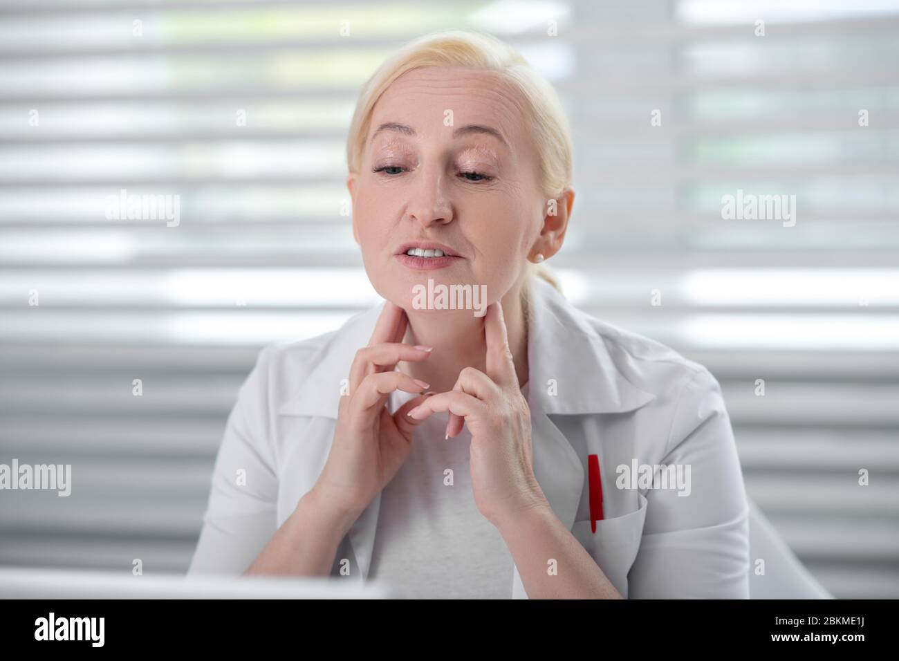 Woman touching hands to neck, looking at monitor Stock Photo - Alamy