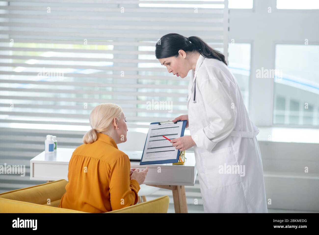 Successful female doctor standing near a seated patient Stock Photo - Alamy