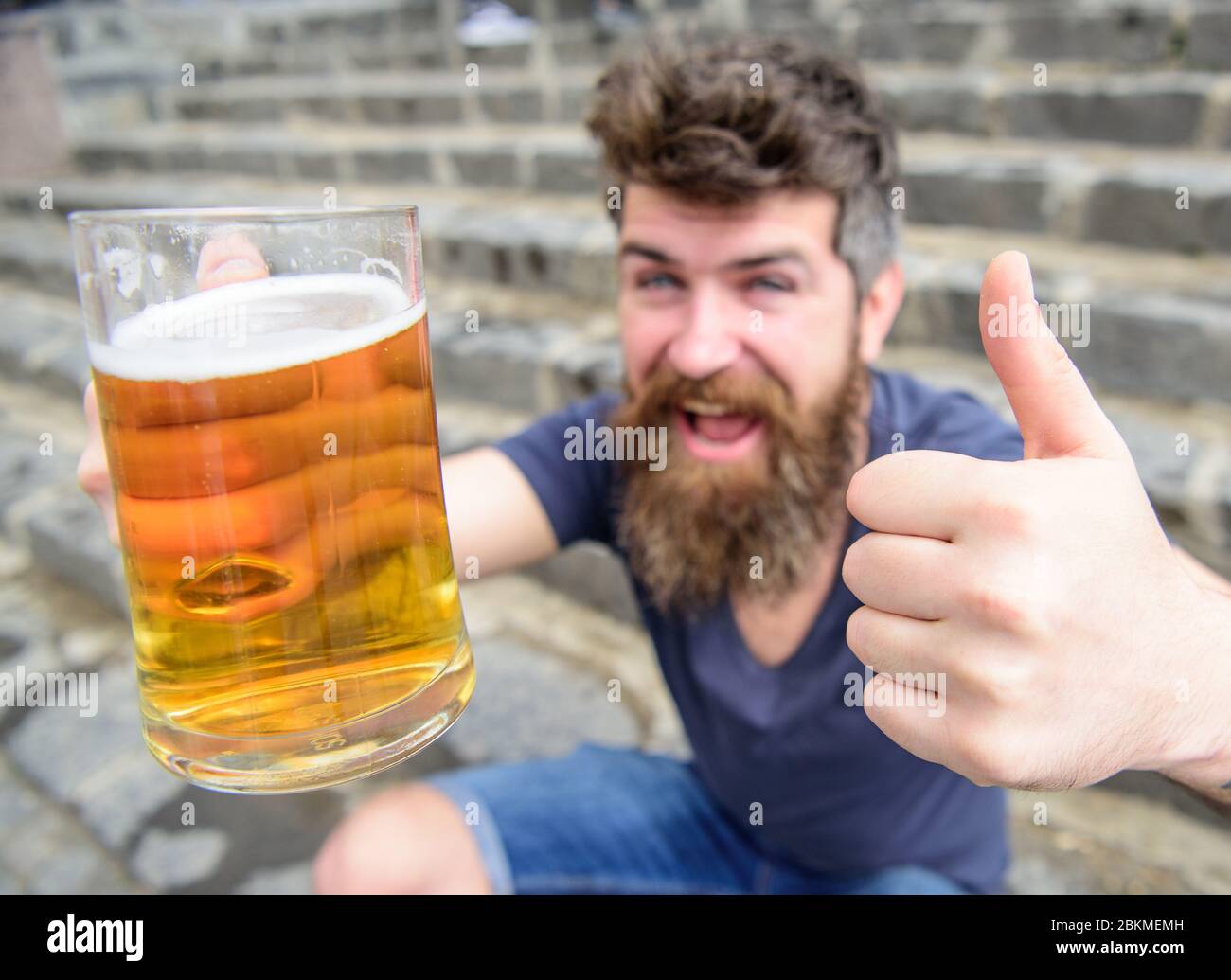 Man with beard and mustache holds glass with beer and shows thumb up ...