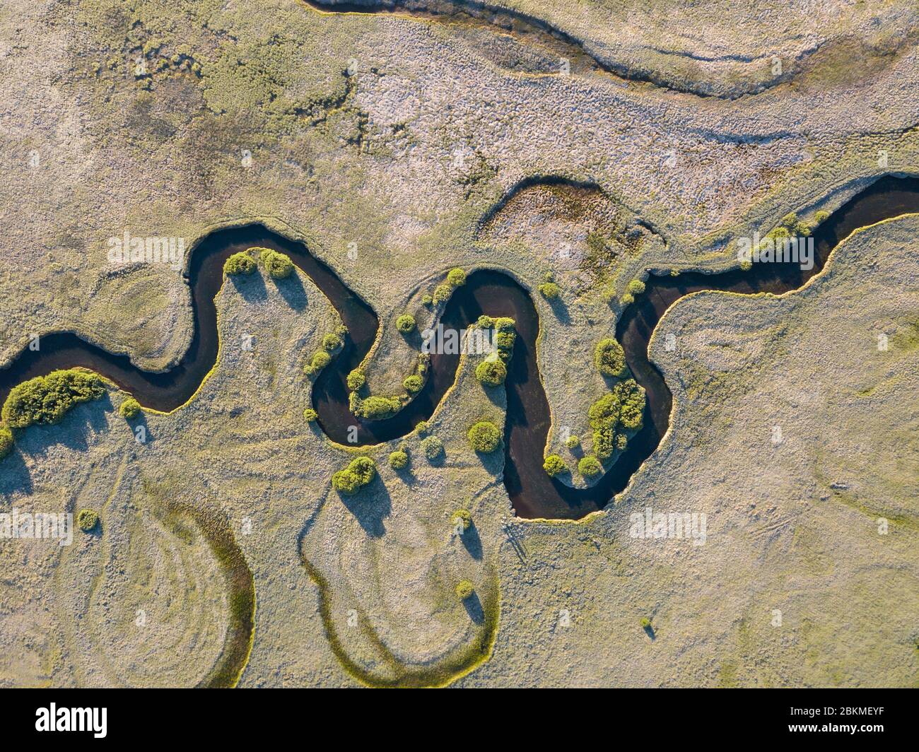 A stream meanders through a green valley, with natural twists and ...