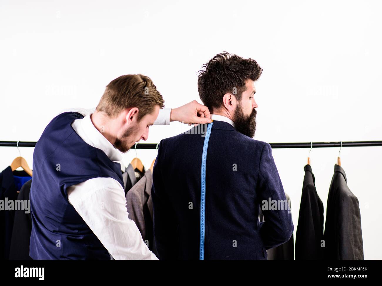 Businessman, client stand near hanger with suits while tailor working ...