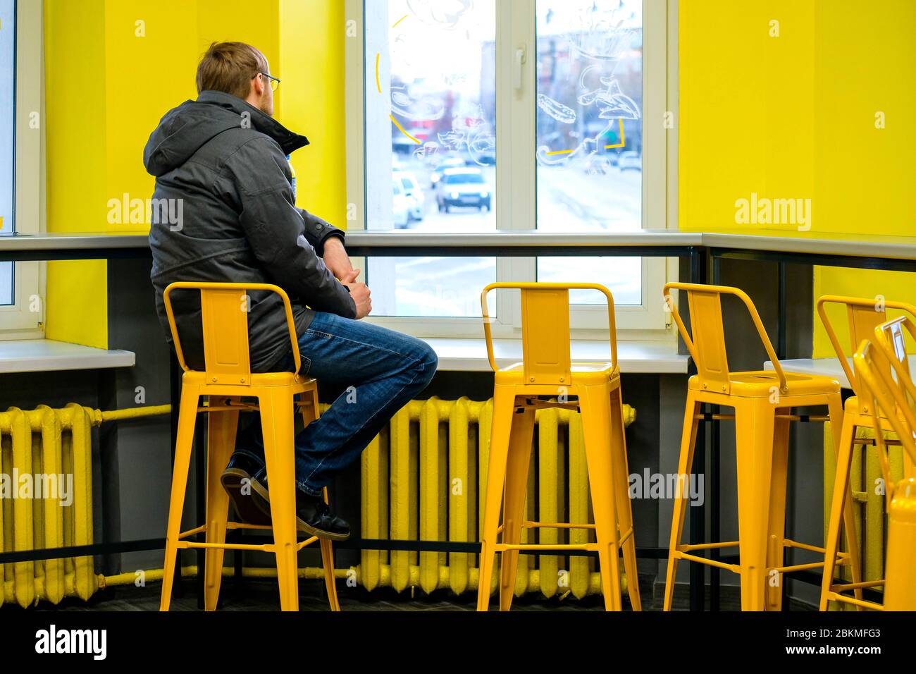 A man sits facing the window, his face is not visible. Yellow cafe ...