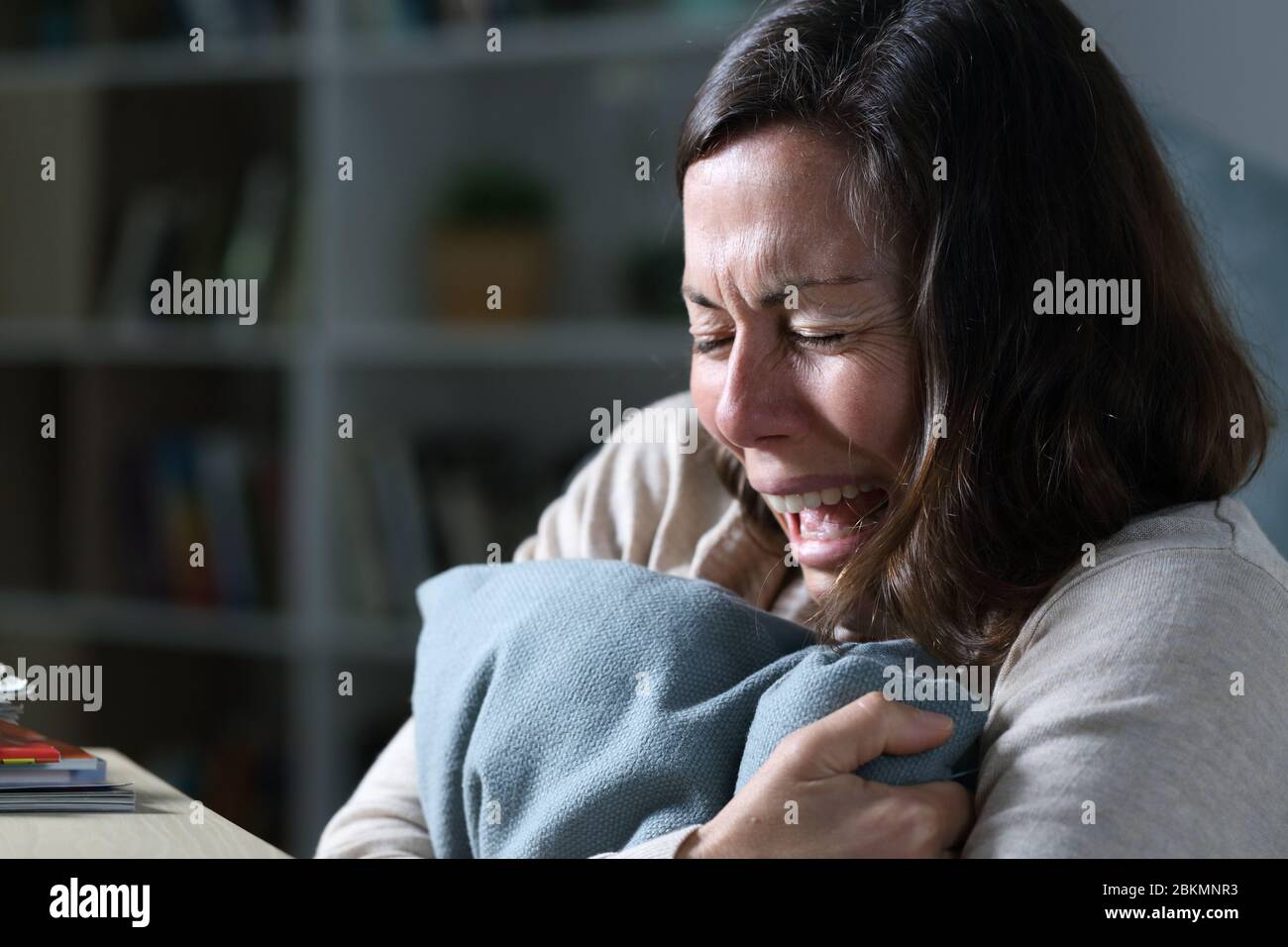 Sad adult woman crying lamenting holding a pillow sitting on the floor ...