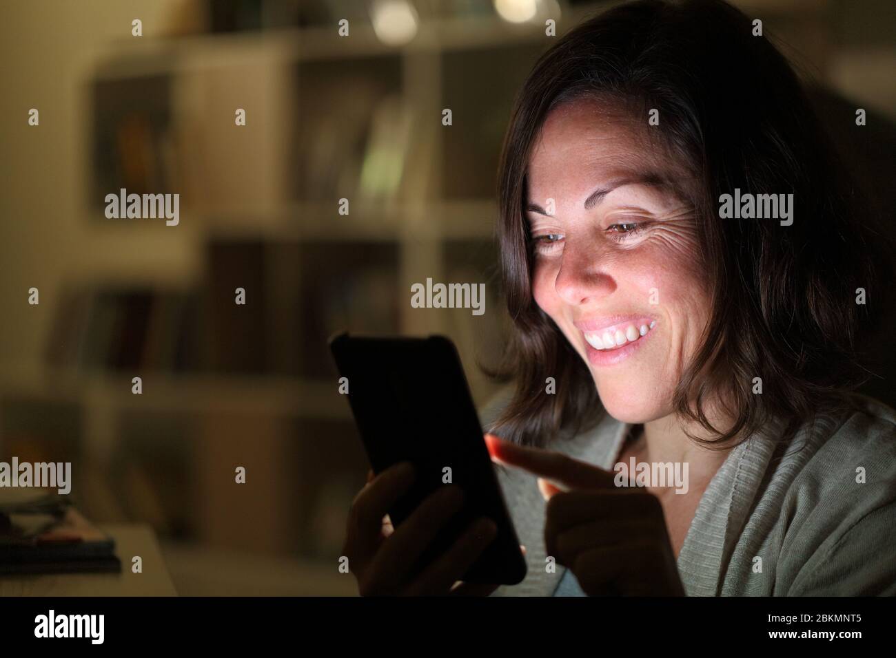 Happy middle age woman using smart phone with lighted screen at night ...