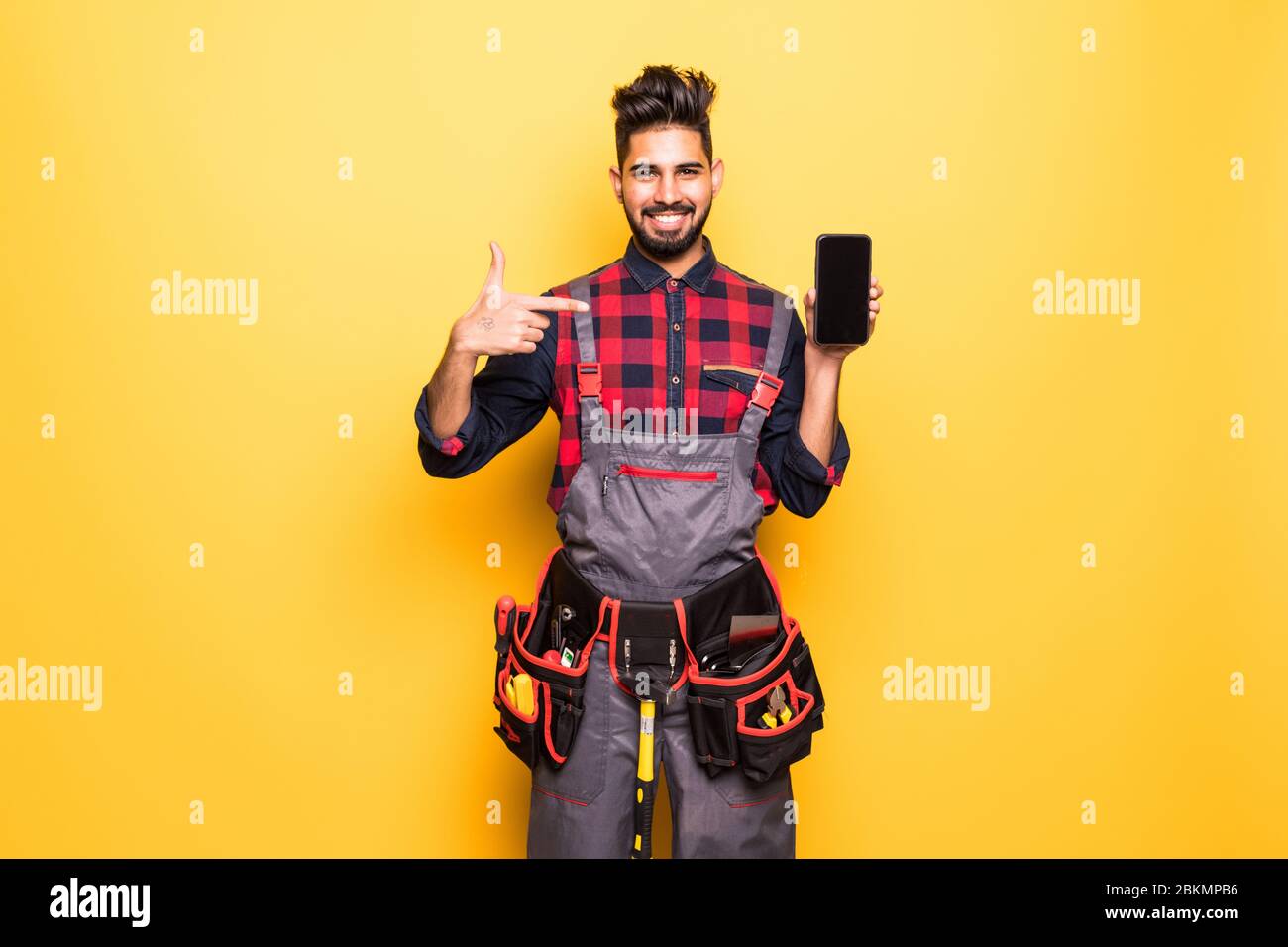 Portrait of indian handyman showing screen of mobile phone on yellow ...