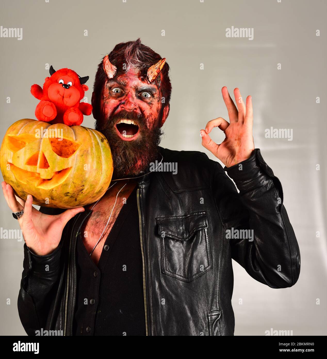 Demon with shocked face holds carved jack o lantern and shows ok sign ...