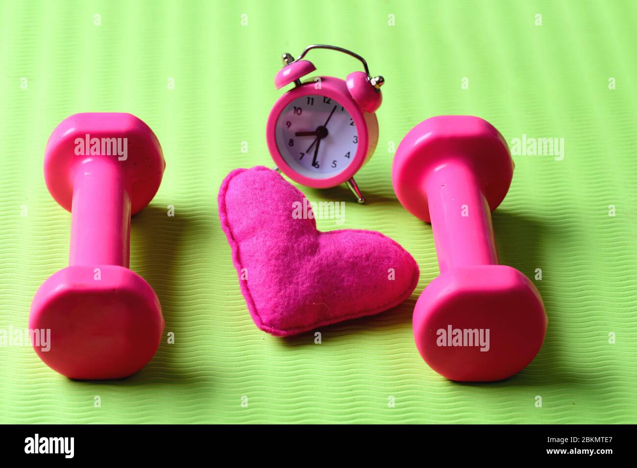Morning workout concept. Dumbbells in pink color next to alarm clock ...
