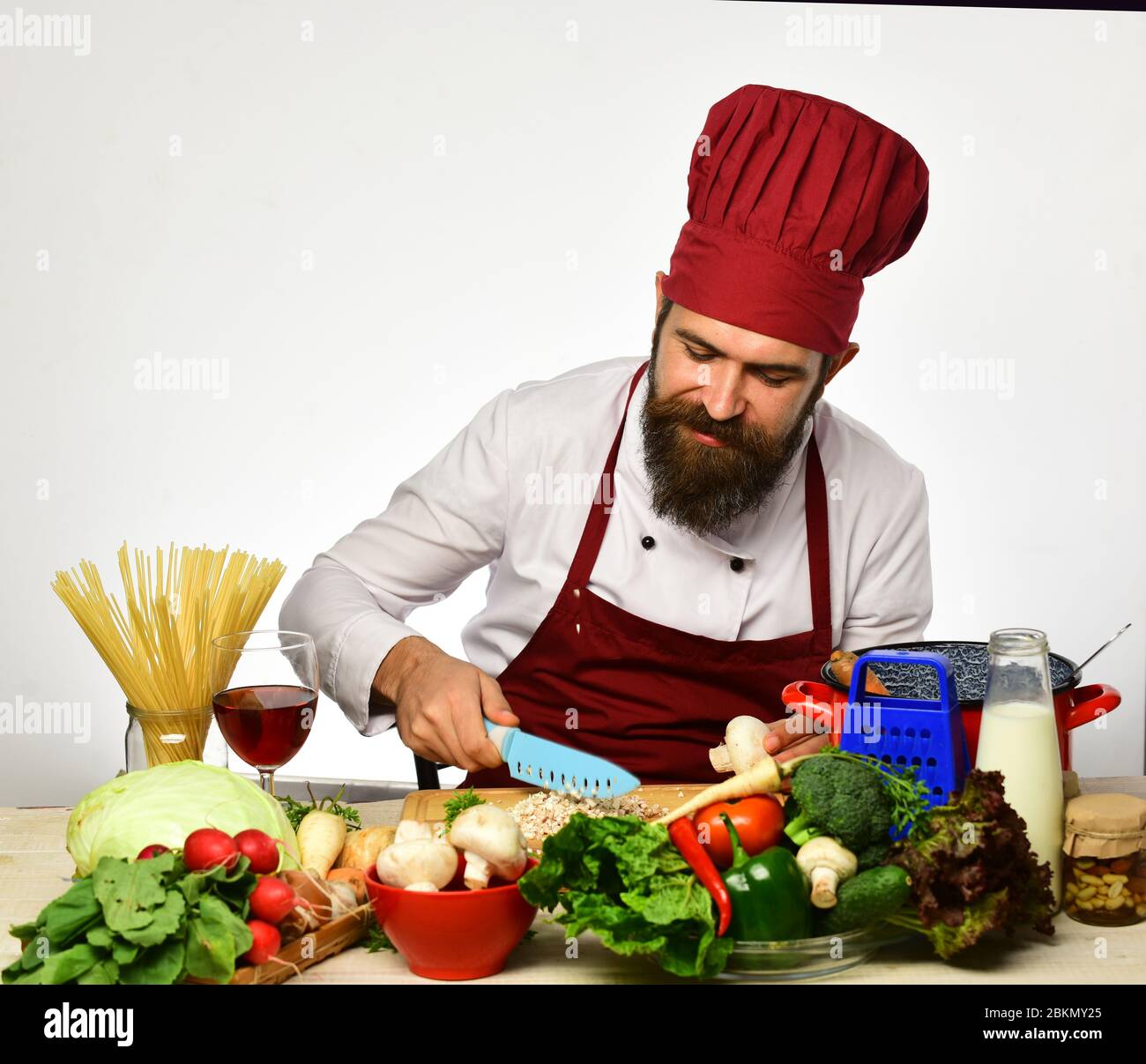 Cook with smiling face in burgundy uniform sits by table with ...