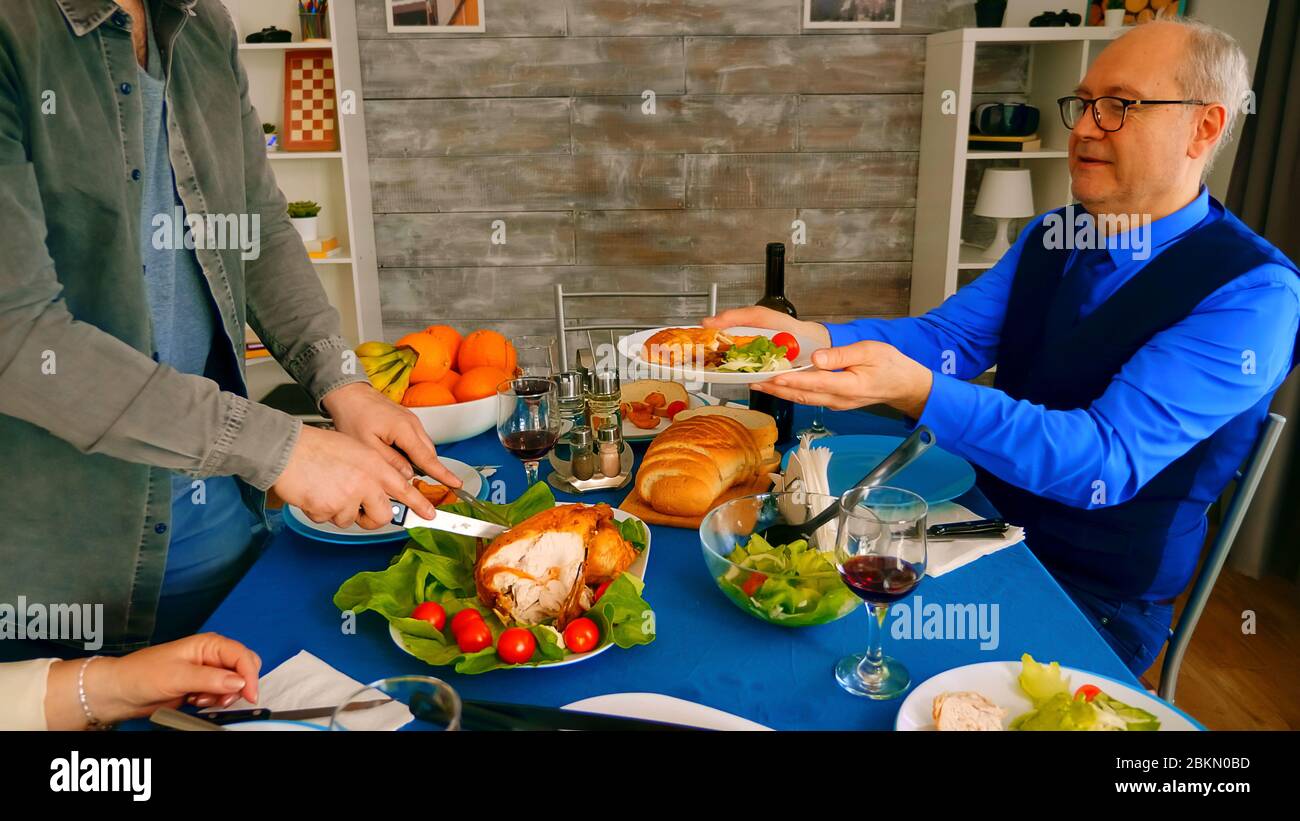 Zoom in shot of man serving his father with chicken at family dinner ...