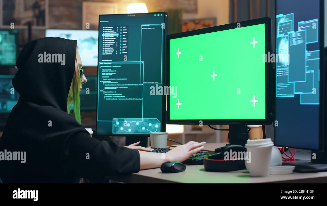 Female cyber terrorist wearing a hoodie working on computer with green ...