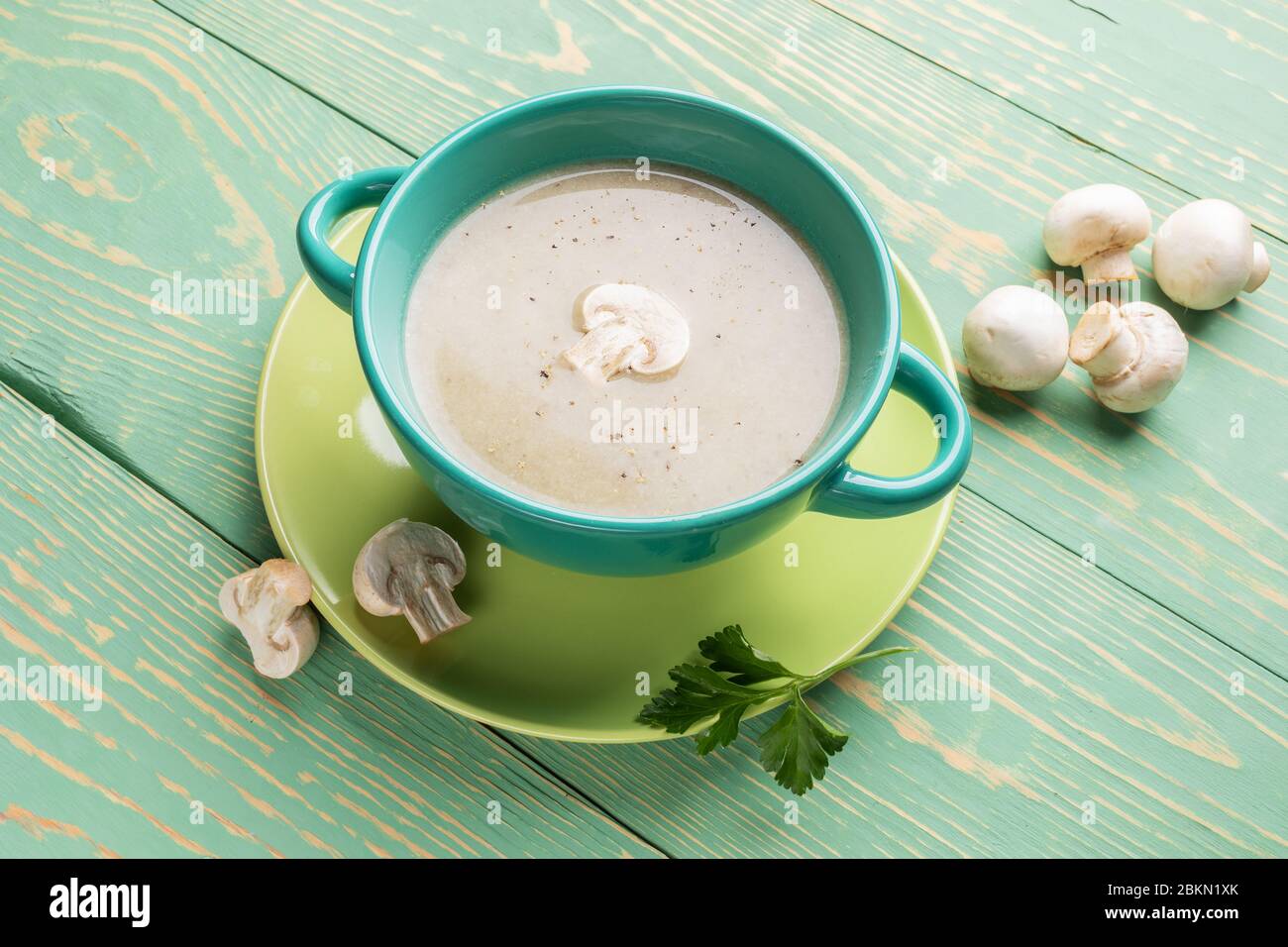 Turquoise ceramic bowl with mushroom cream soup, fresh mushroons and parsley on green plate on ...
