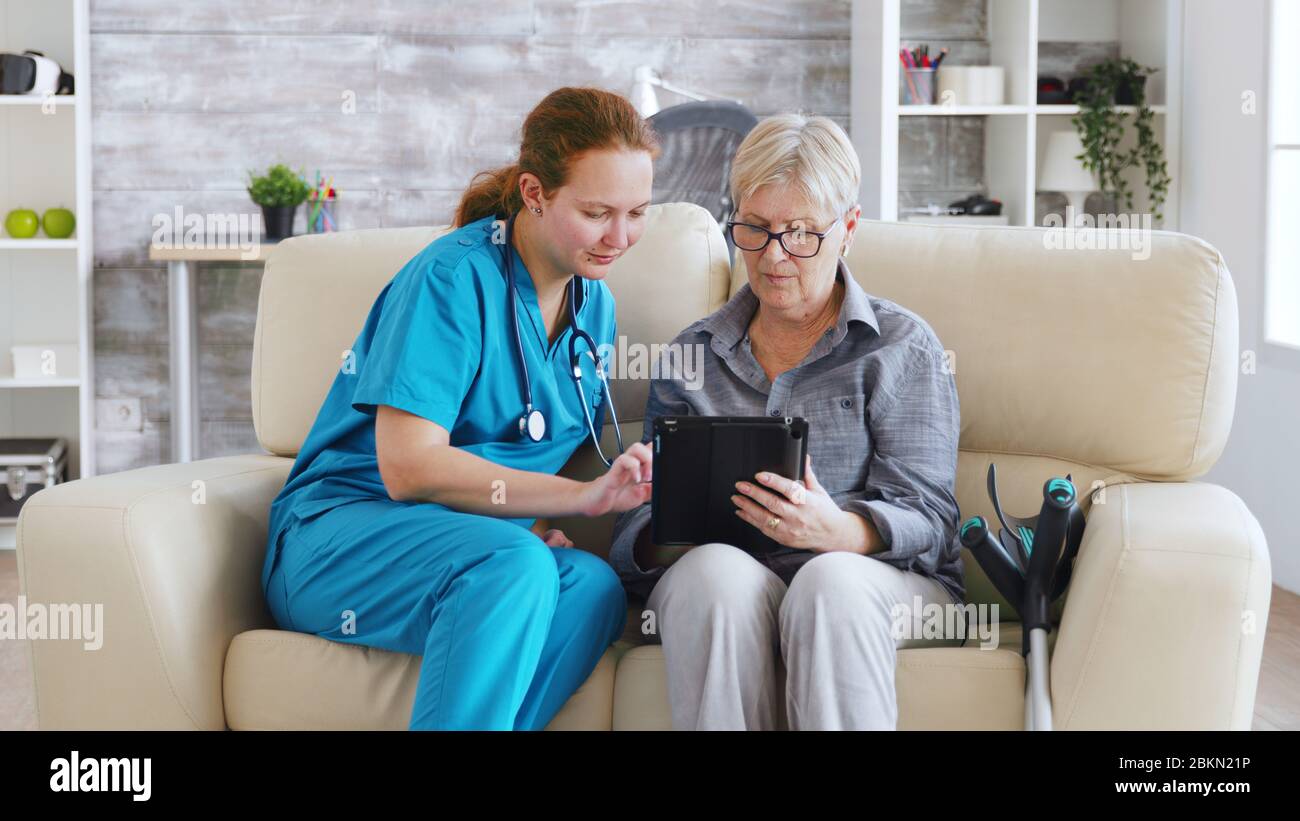 Female nuse helping senior elderly retired woman how to use her tablet ...