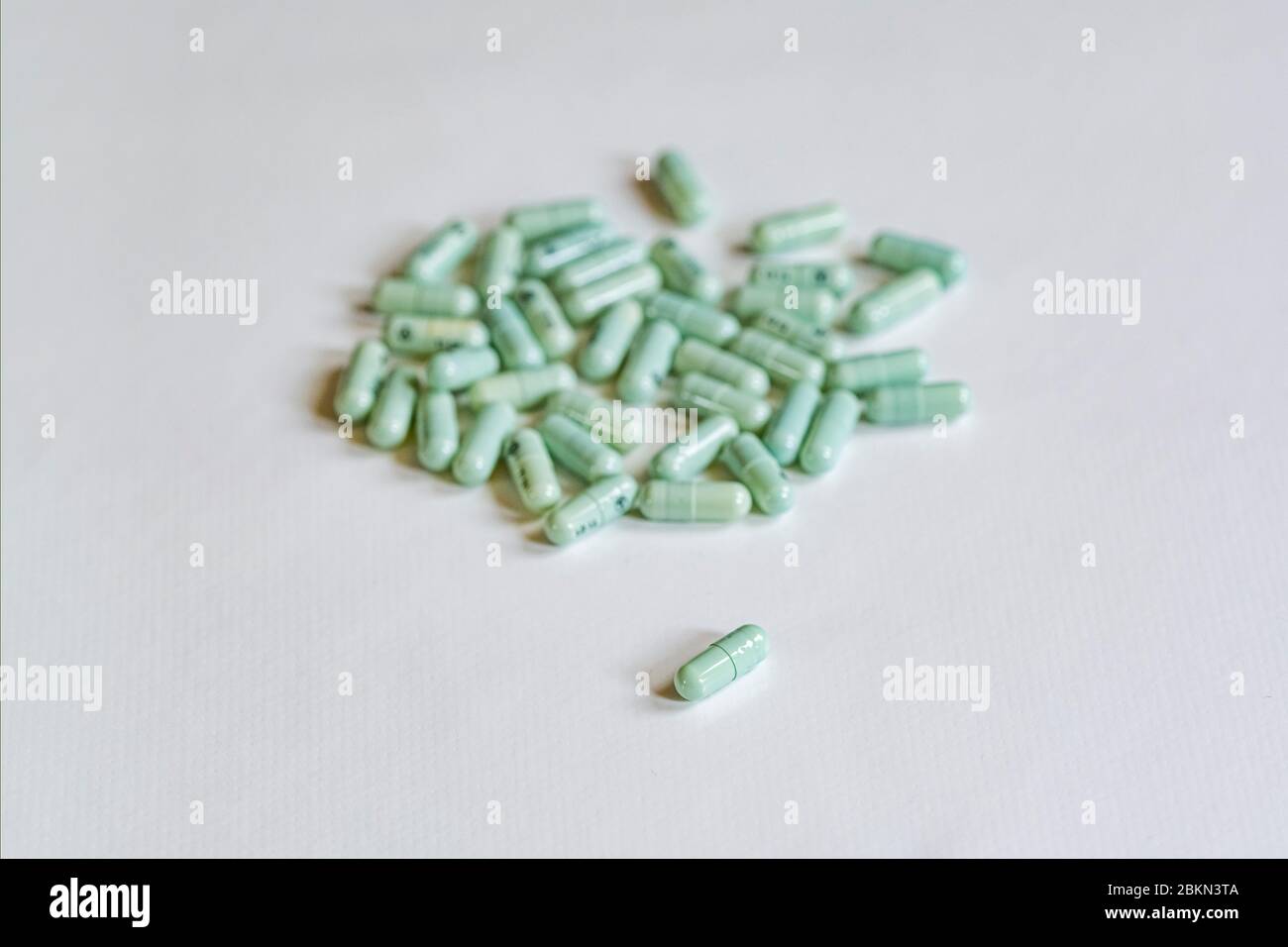 A small heap of light green medical capsules, one capsule separated ...